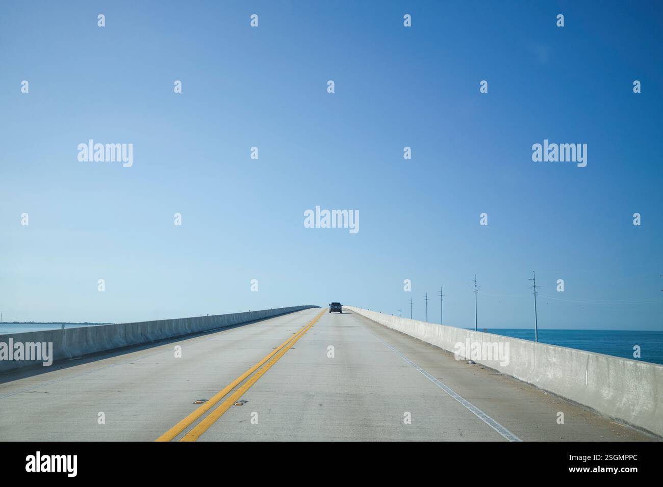 Long concrete bridge over ocean with single vehicle under clear blue ...