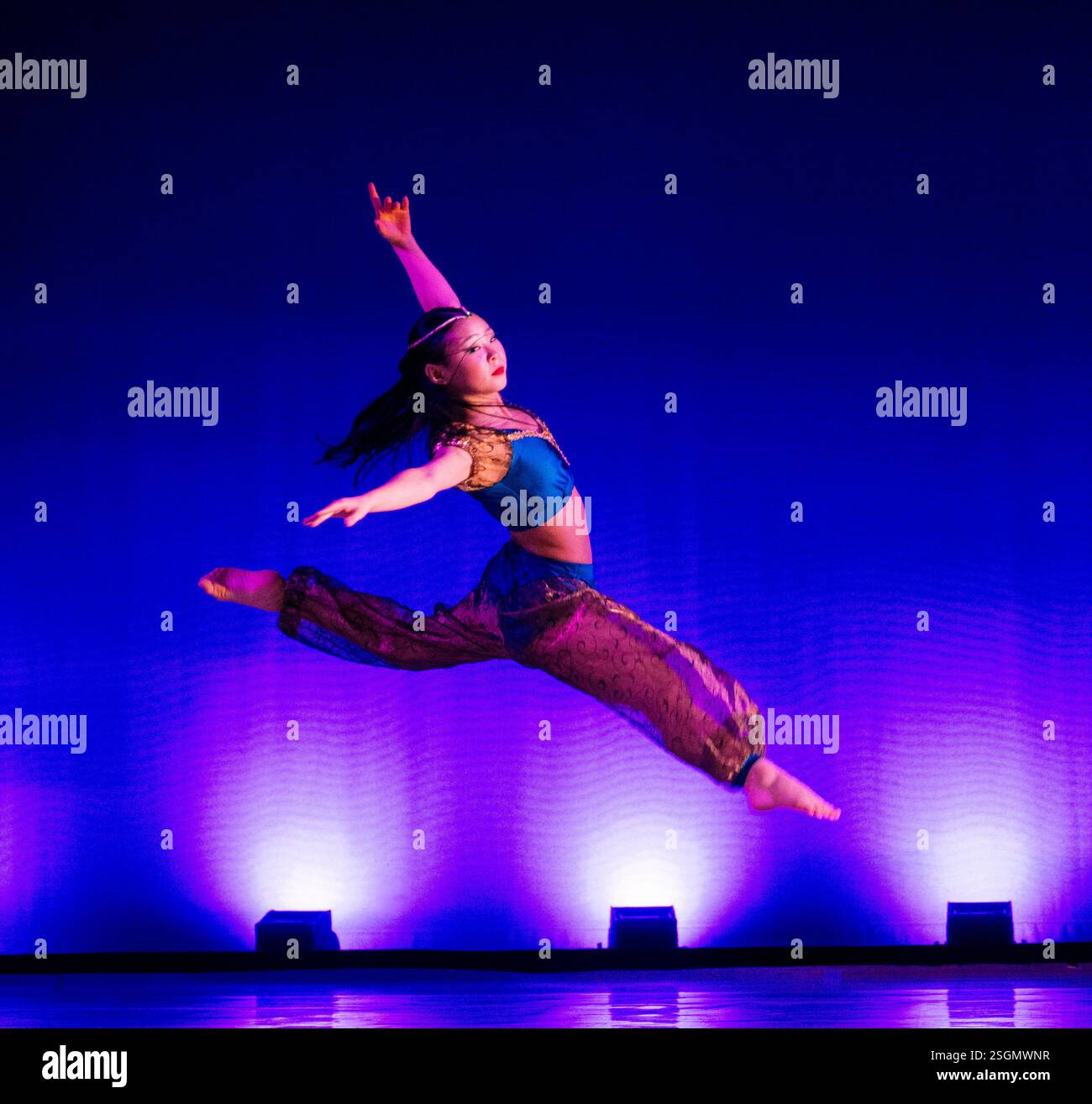 Dancer in mid-air leap wearing colorful costume against vibrant blue ...