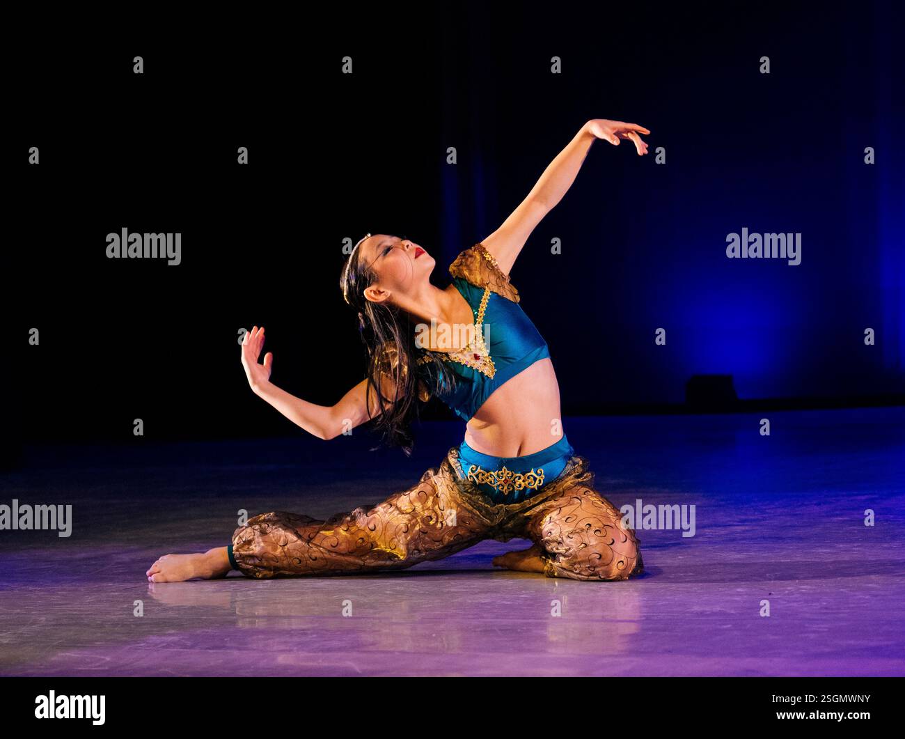 Dancer elegantly poses on stage with vibrant blue and gold costume ...
