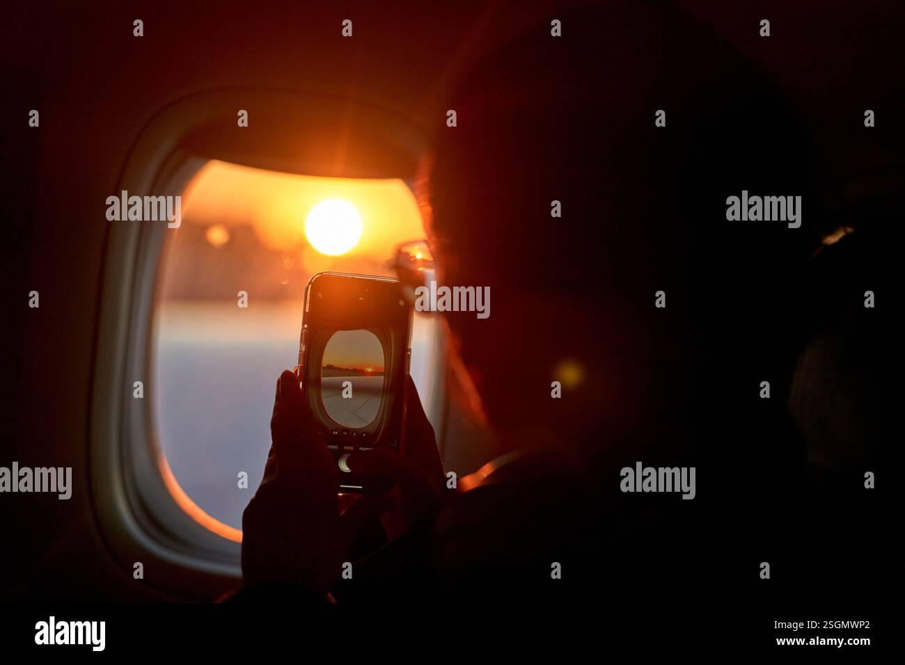 Silhouette of woman taking a photo of sunset through airplane window ...