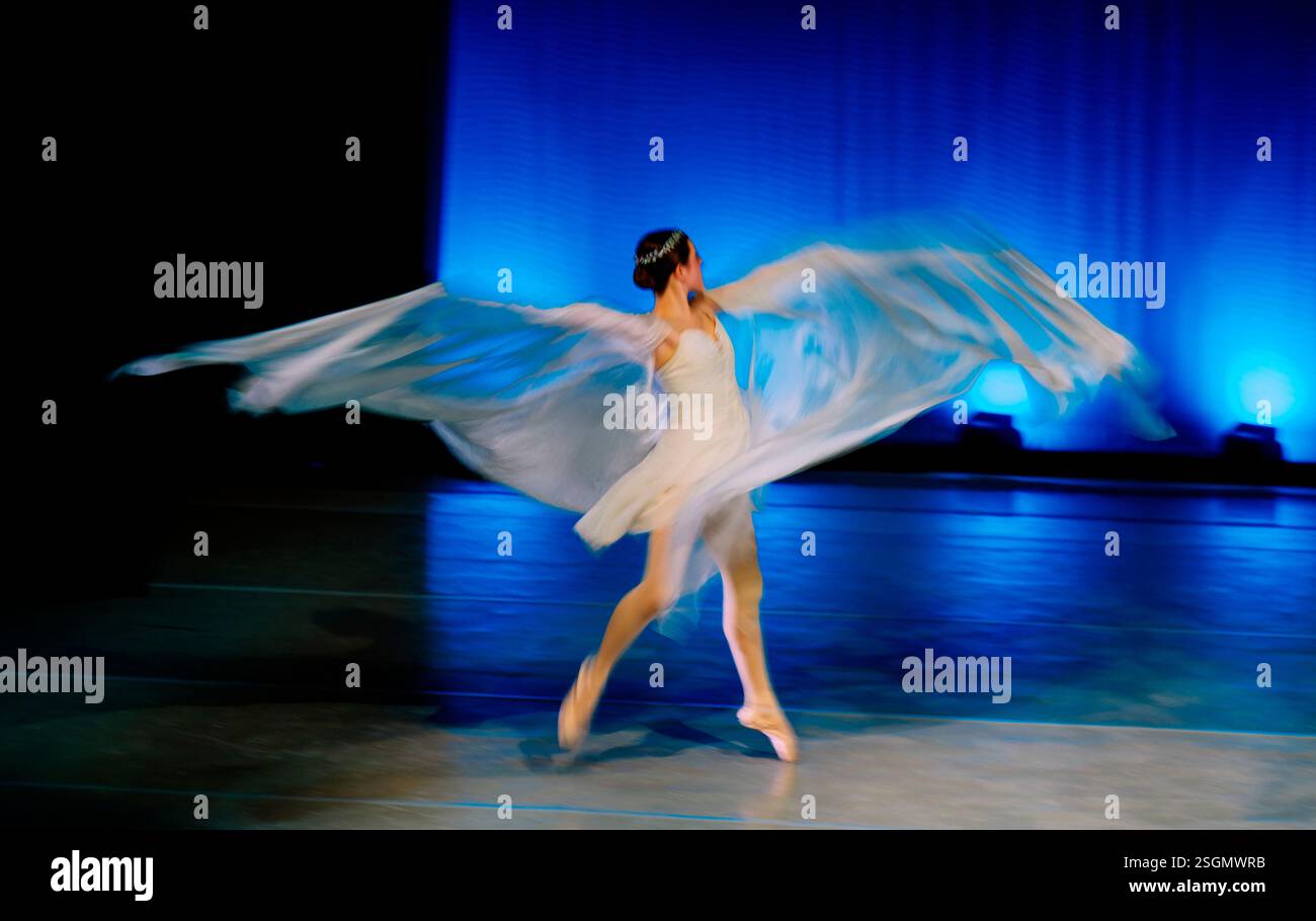 Ballerina in motion with flowing white costume against a blue-lit ...