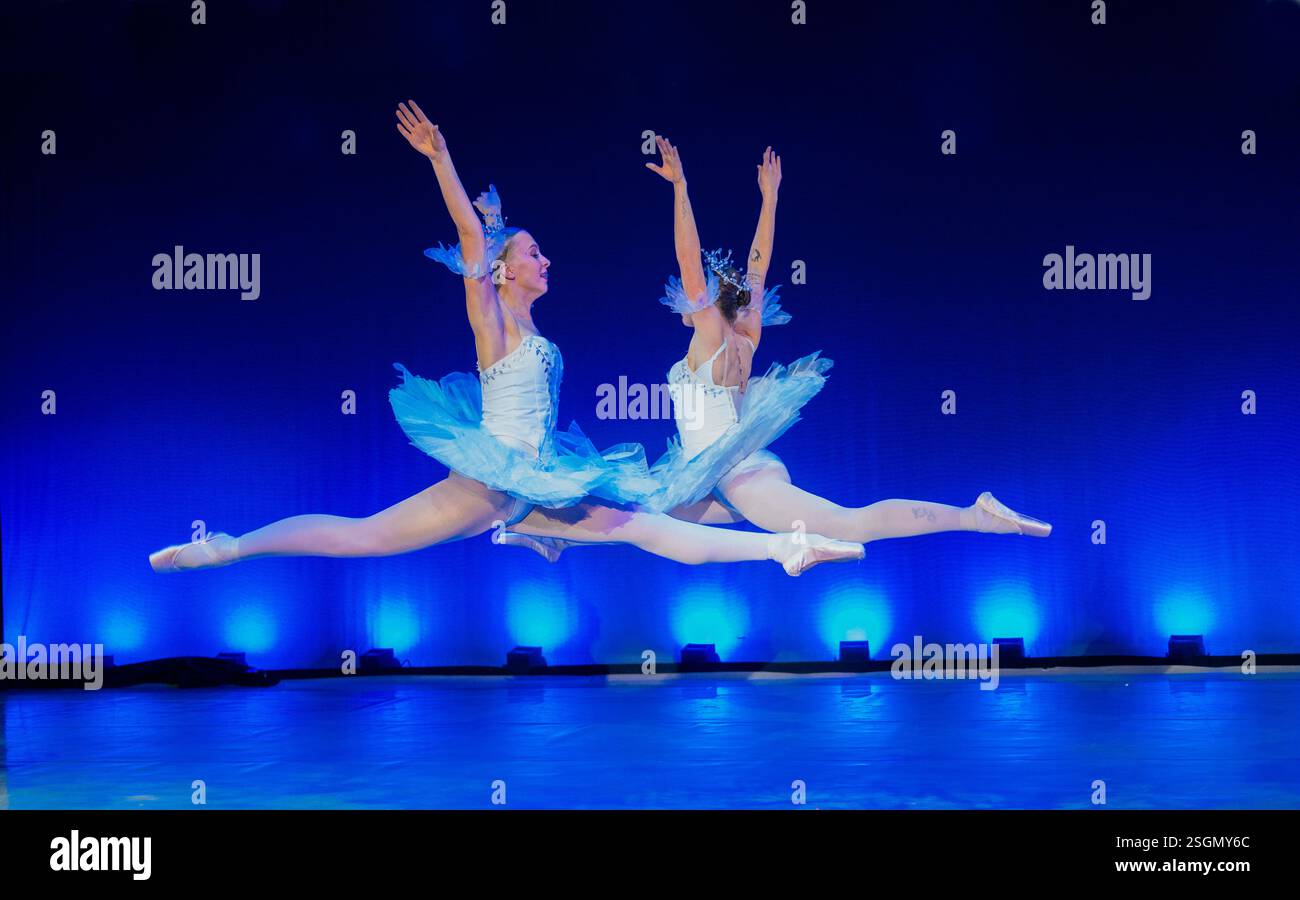 Two ballerinas in blue tutus perform ballet leaps on stage with ...