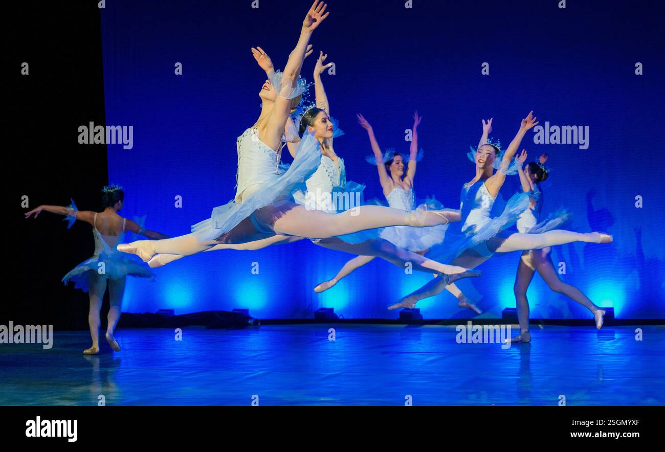 Ballet dancers in tutus perform a synchronized leap on a stage with ...