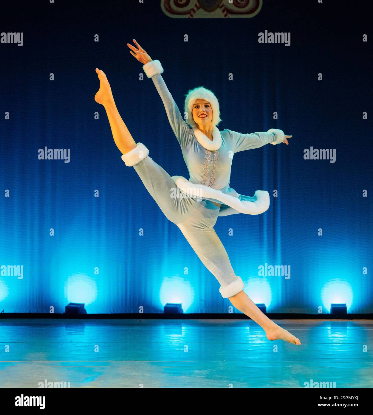 Dancer in costume performs high jump on stage with blue lighting ...