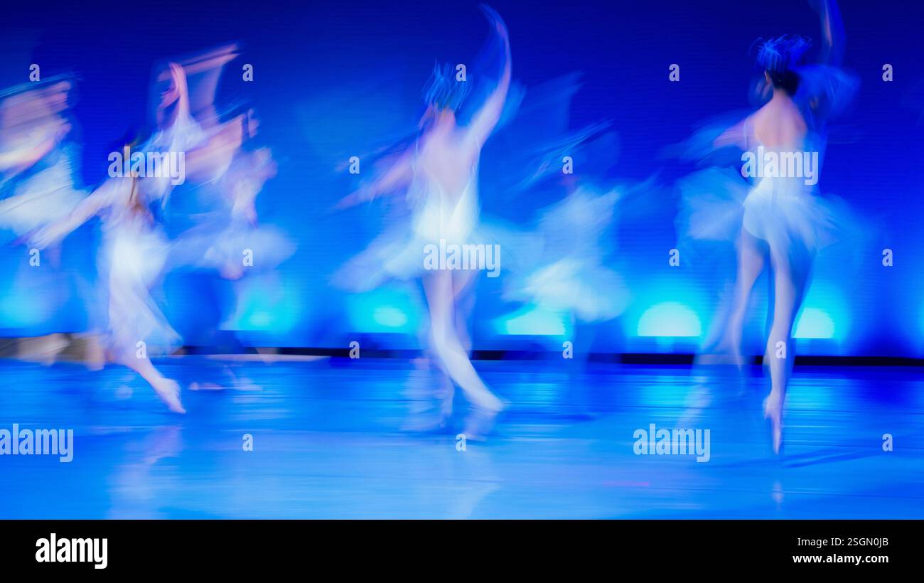 Blurred dancers in motion with blue lighting on stage and soft shadows ...
