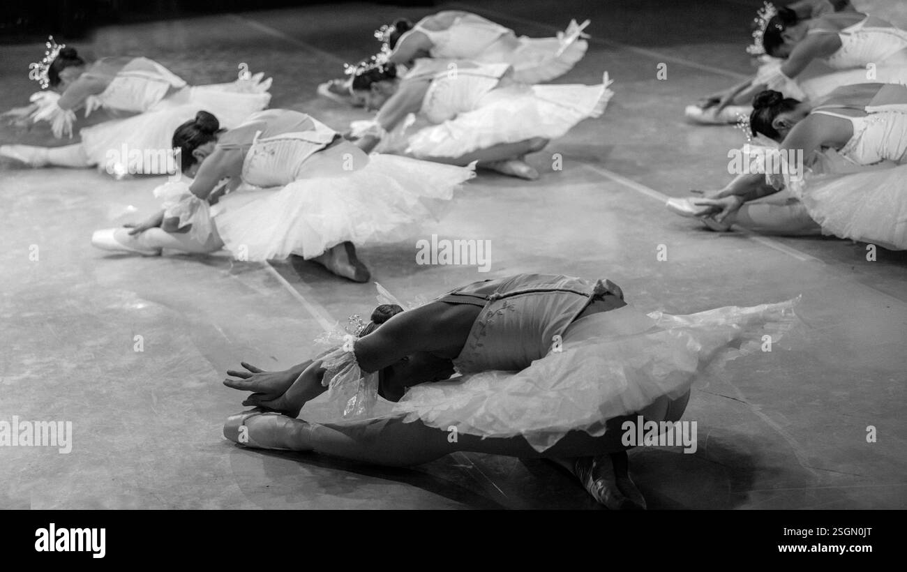 Ballerinas in white tutus gracefully stretch on a dance studio floor ...