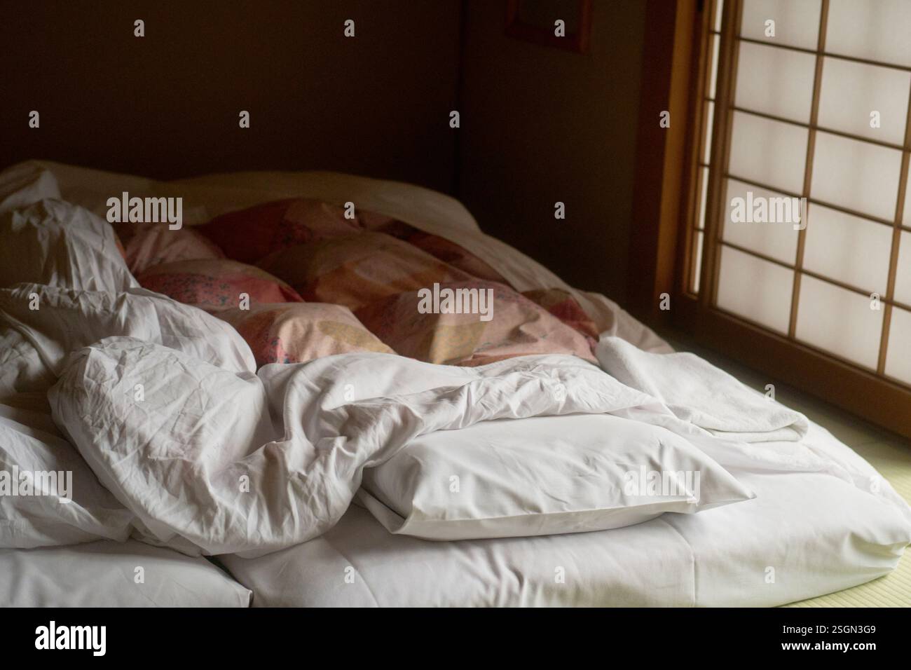 Cozy futon bed with rumpled white sheets in a traditional Japanese room ...