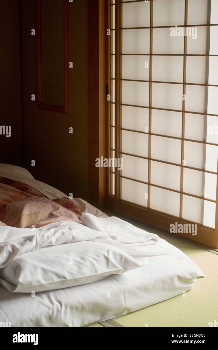 Sunlight filters through a shoji screen, illuminating a neatly made ...