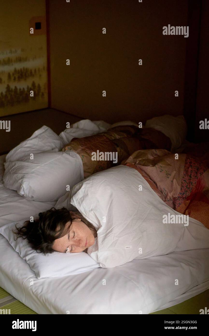 Woman sleeping comfortably on a futon bed in a dimly lit Japanese-style ...