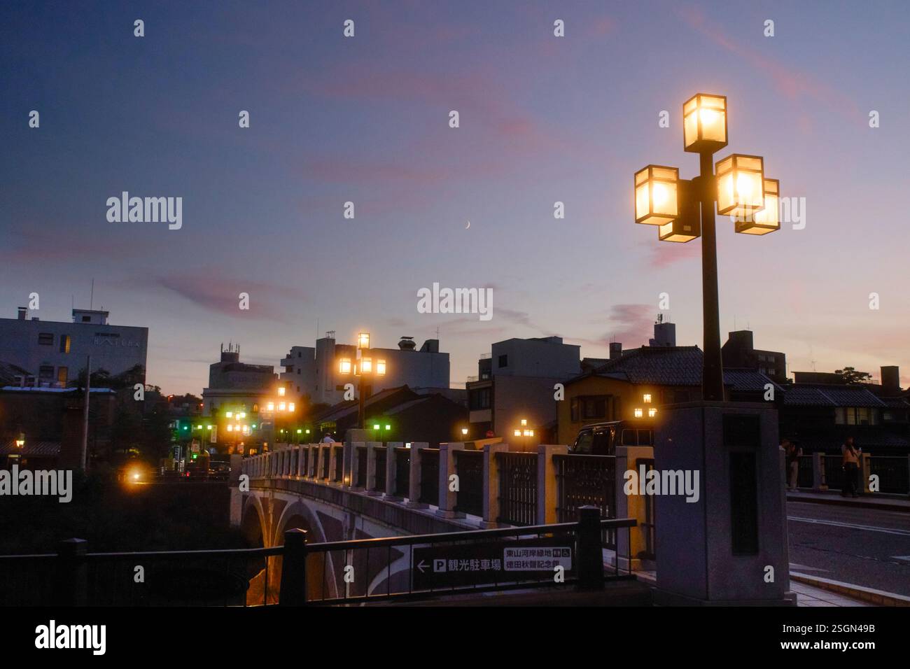 Evening view of a lit bridge and street lamps with city skyline at dusk ...