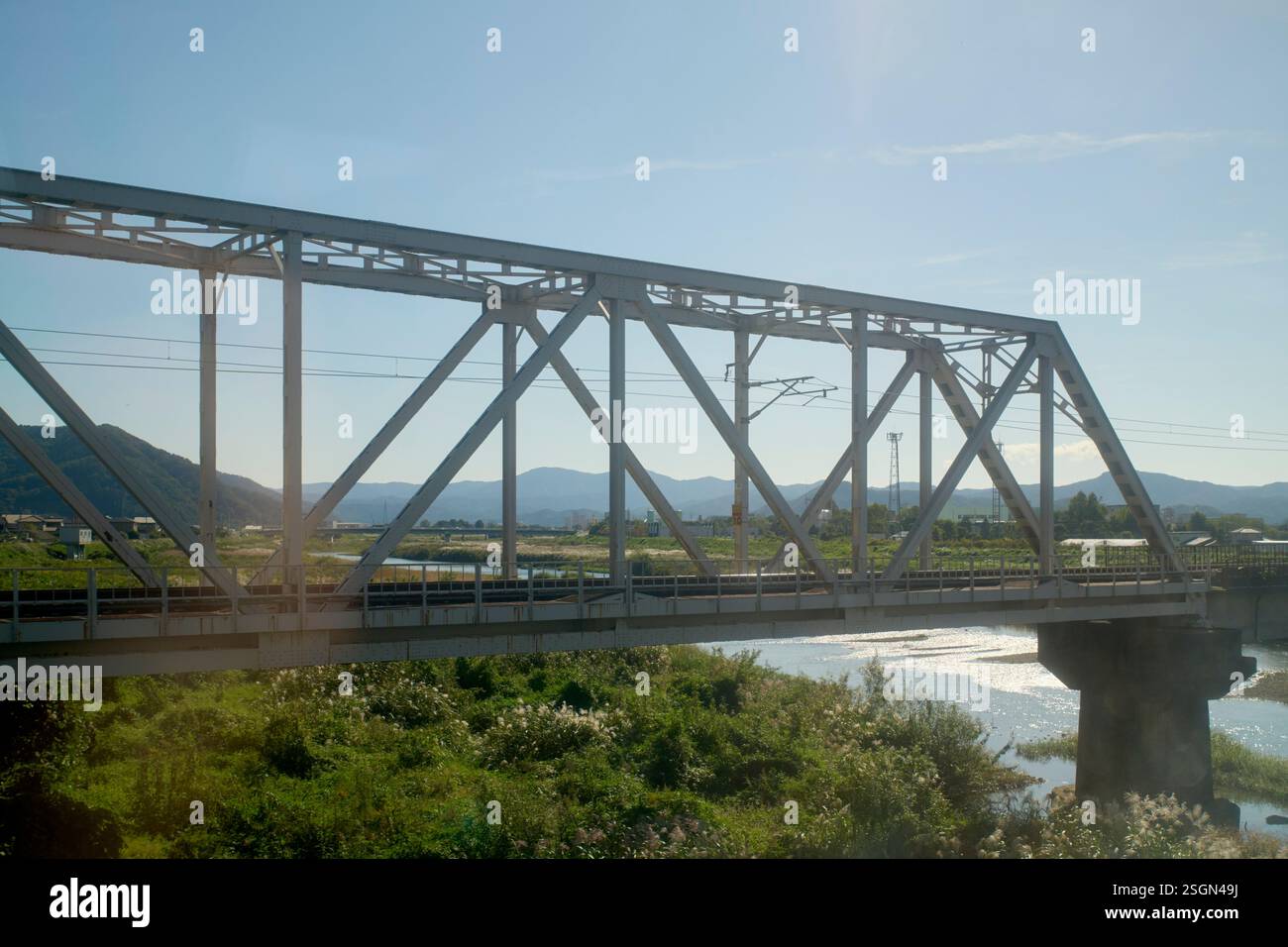 Steel bridge over a river with mountains and greenery under a clear ...