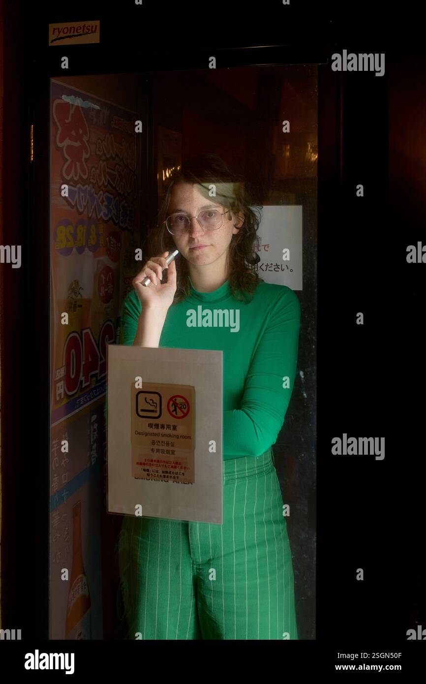 Woman in green outfit stands and smokes inside a smoking cabin ...