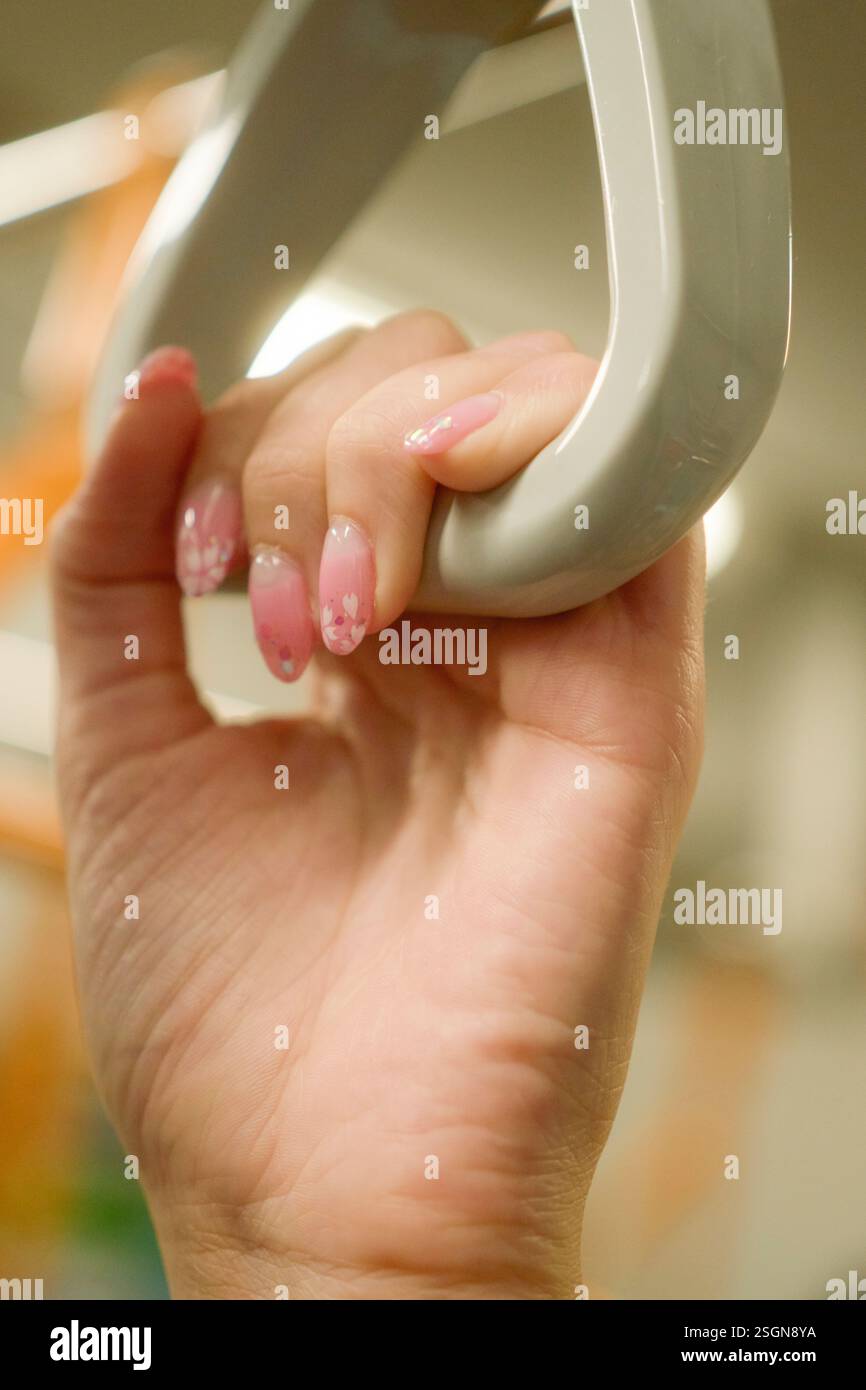Hand with pink manicured nails holding a handrail inside a train or bus ...