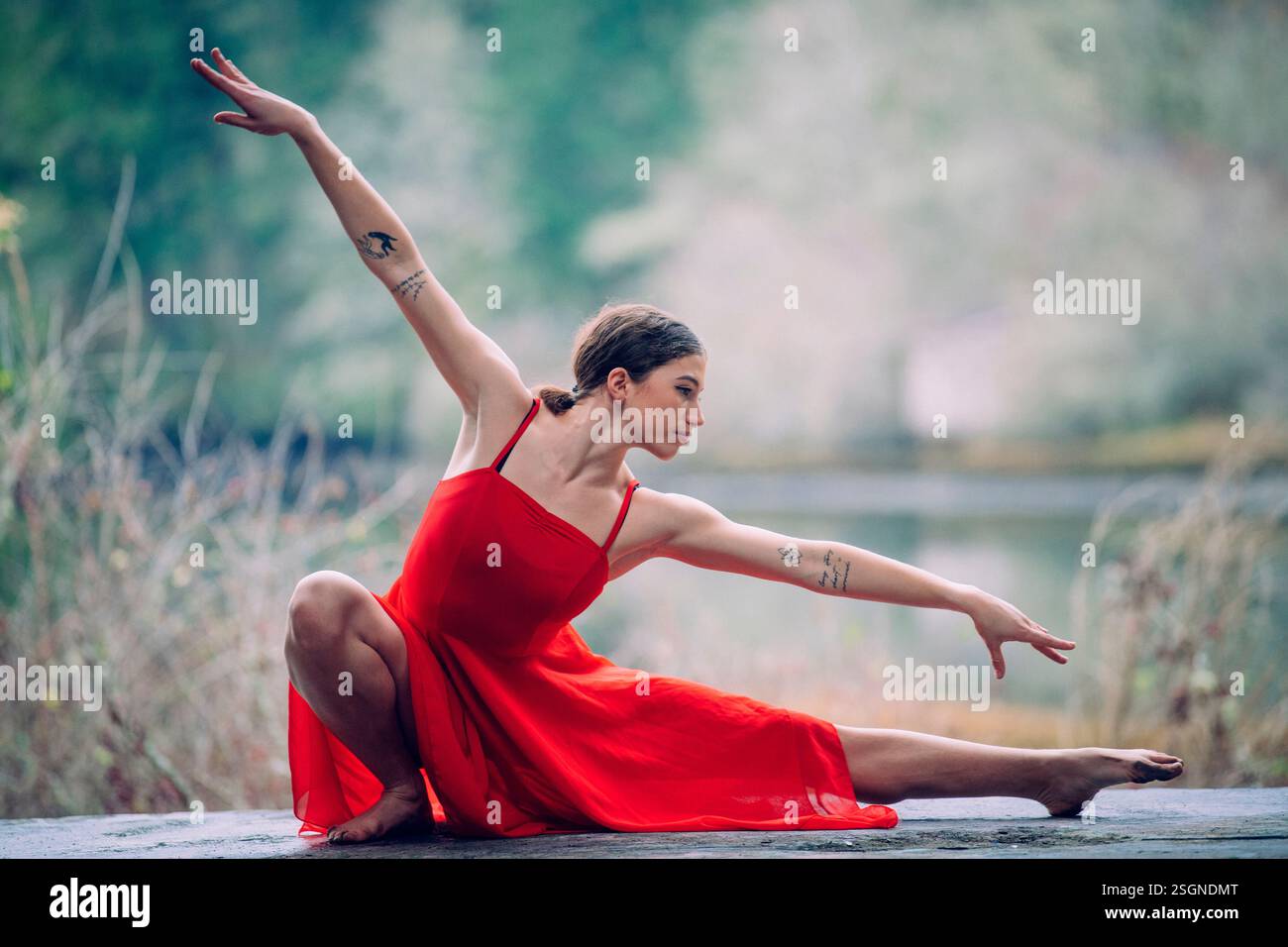 Woman in a red dress gracefully poses outdoors, extending legs and arms ...