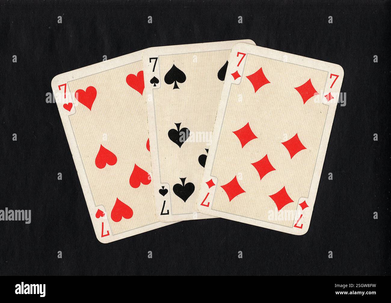 A hand of vintage playing cards showing three sevens isolated on a ...