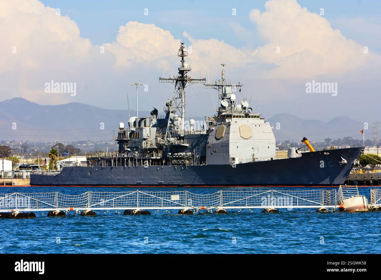 Large navy ship is docked at a pier. The sky is cloudy and the water is ...