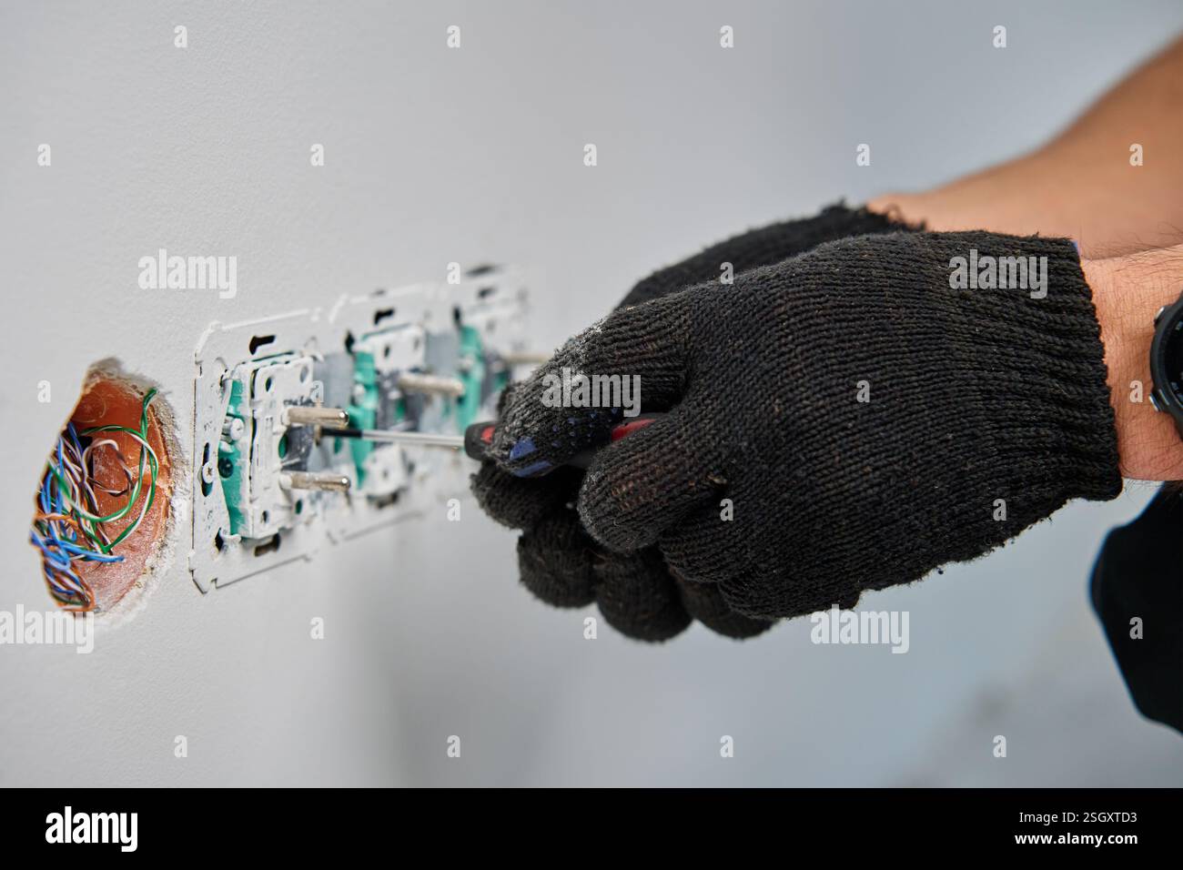 Close-up of an electrician wearing black gloves installing power socket ...