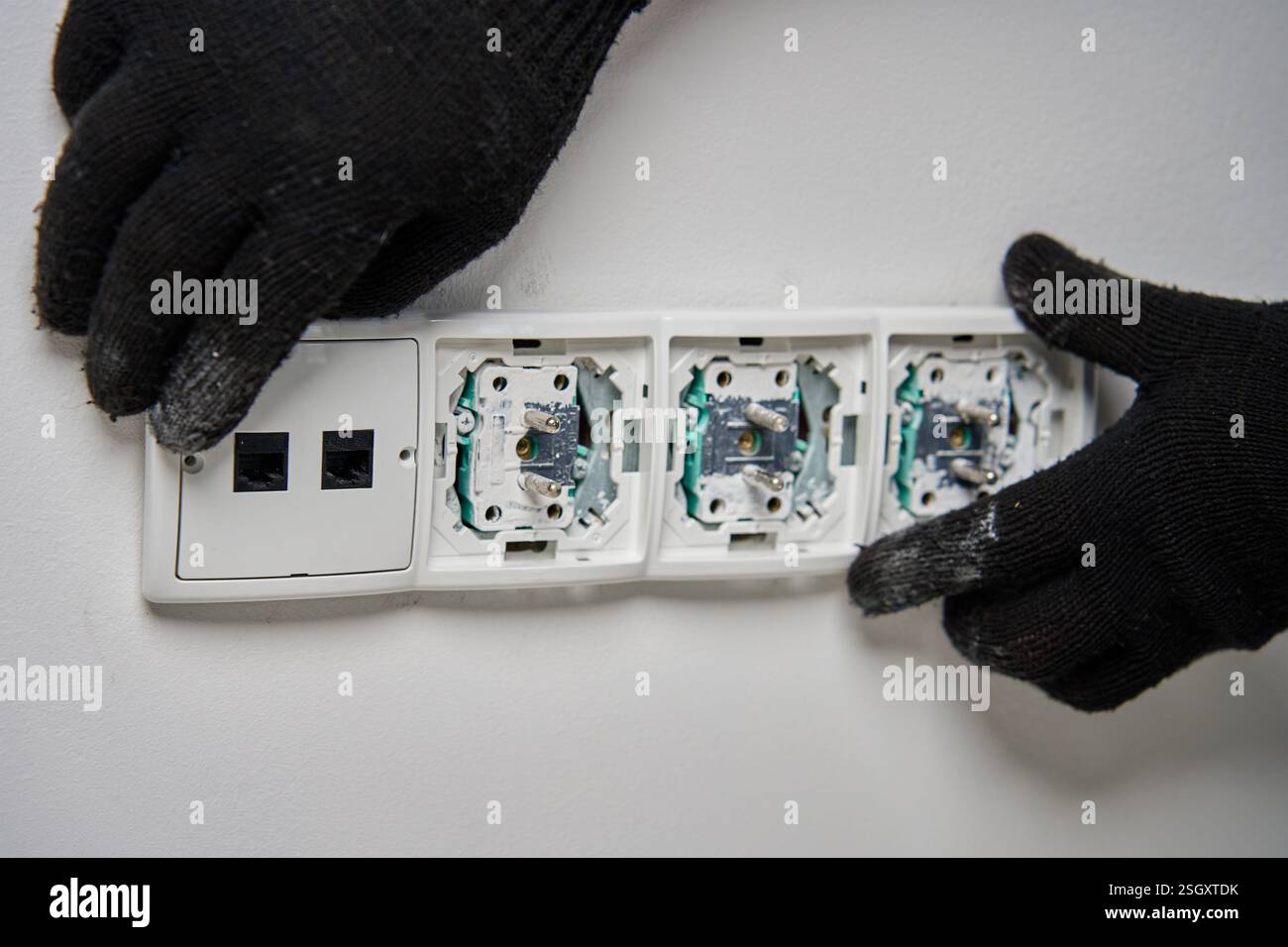 Close-up of an electrician wearing black gloves installing power socket ...