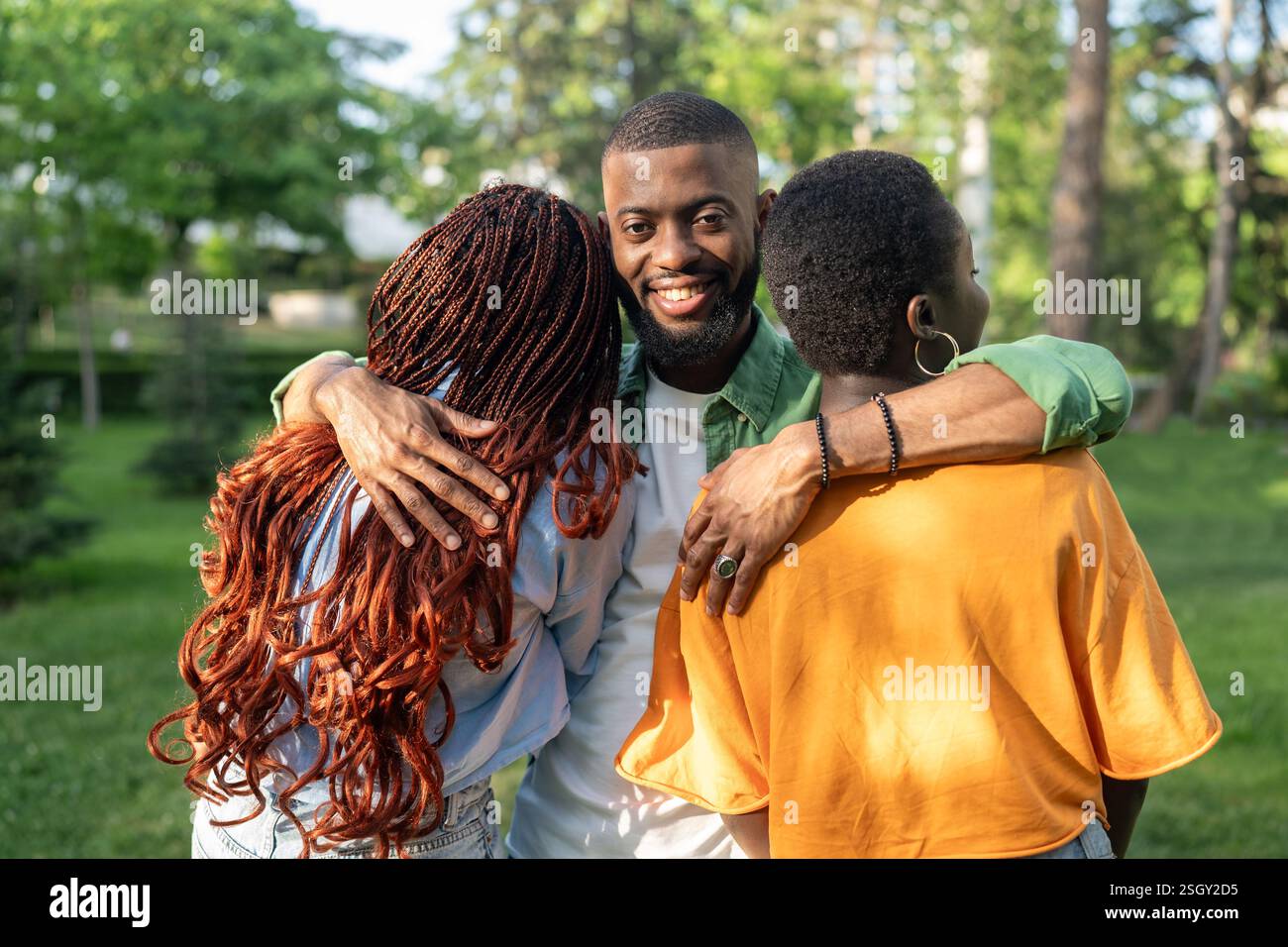 Cunning African American man hugs two women with backs to camera ...