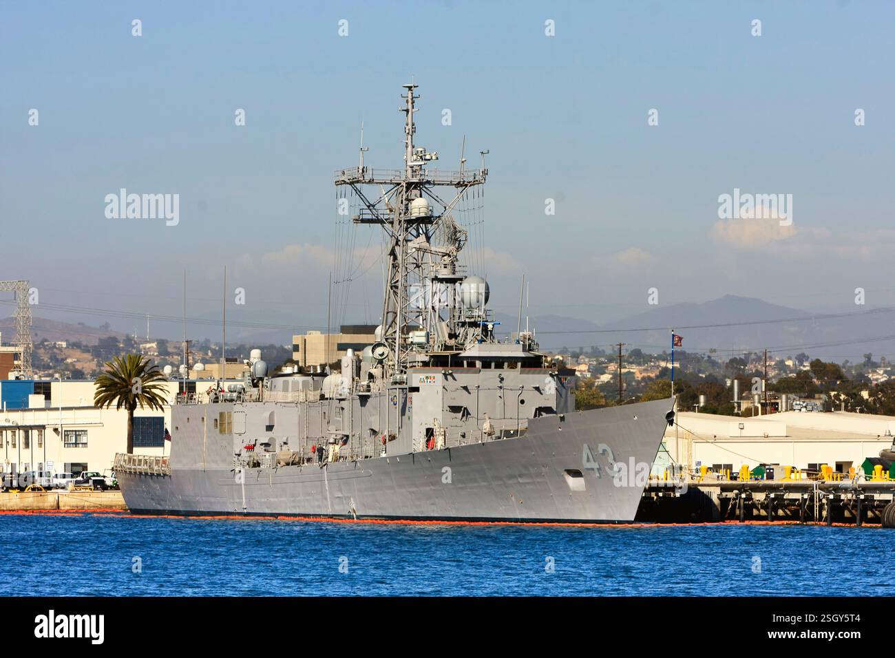Large navy ship is docked at a pier. The sky is clear and the water is ...