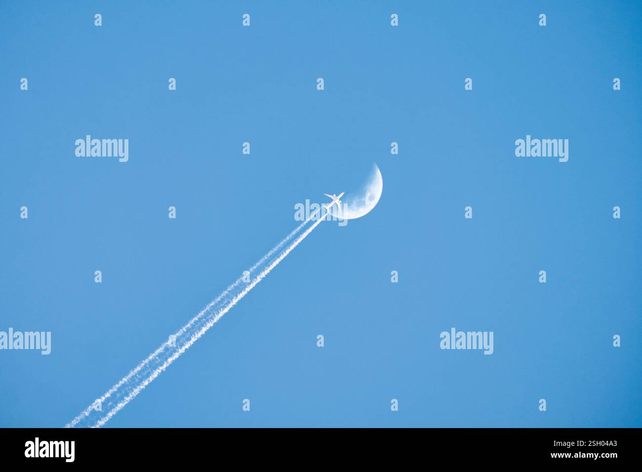 An airplane soars high in the blue sky, leaving white contrails as it ...