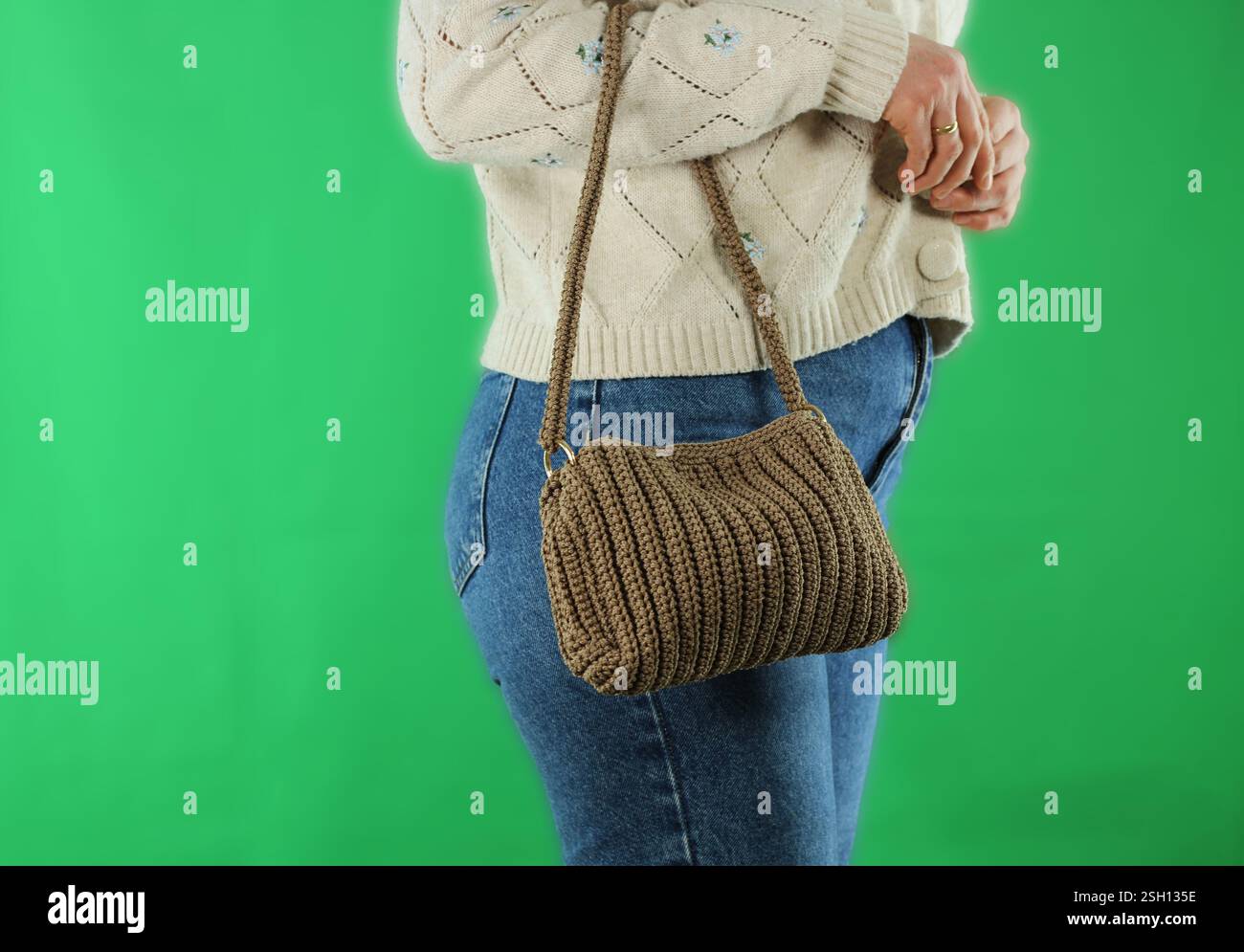 Woman with brown knitted bag hanging on arm in front of green ...