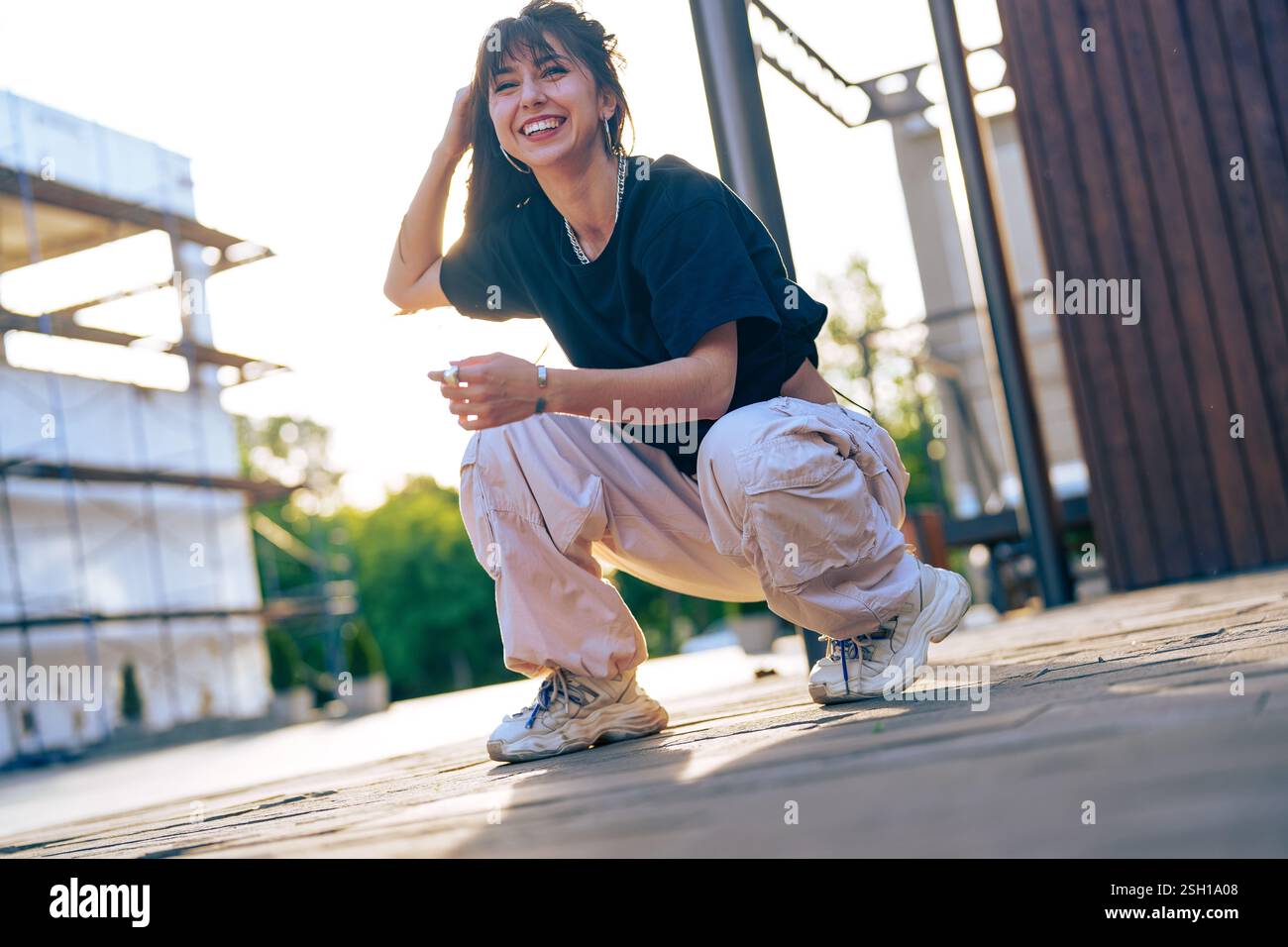 Joyful young woman squatting outdoors during golden hour with ...