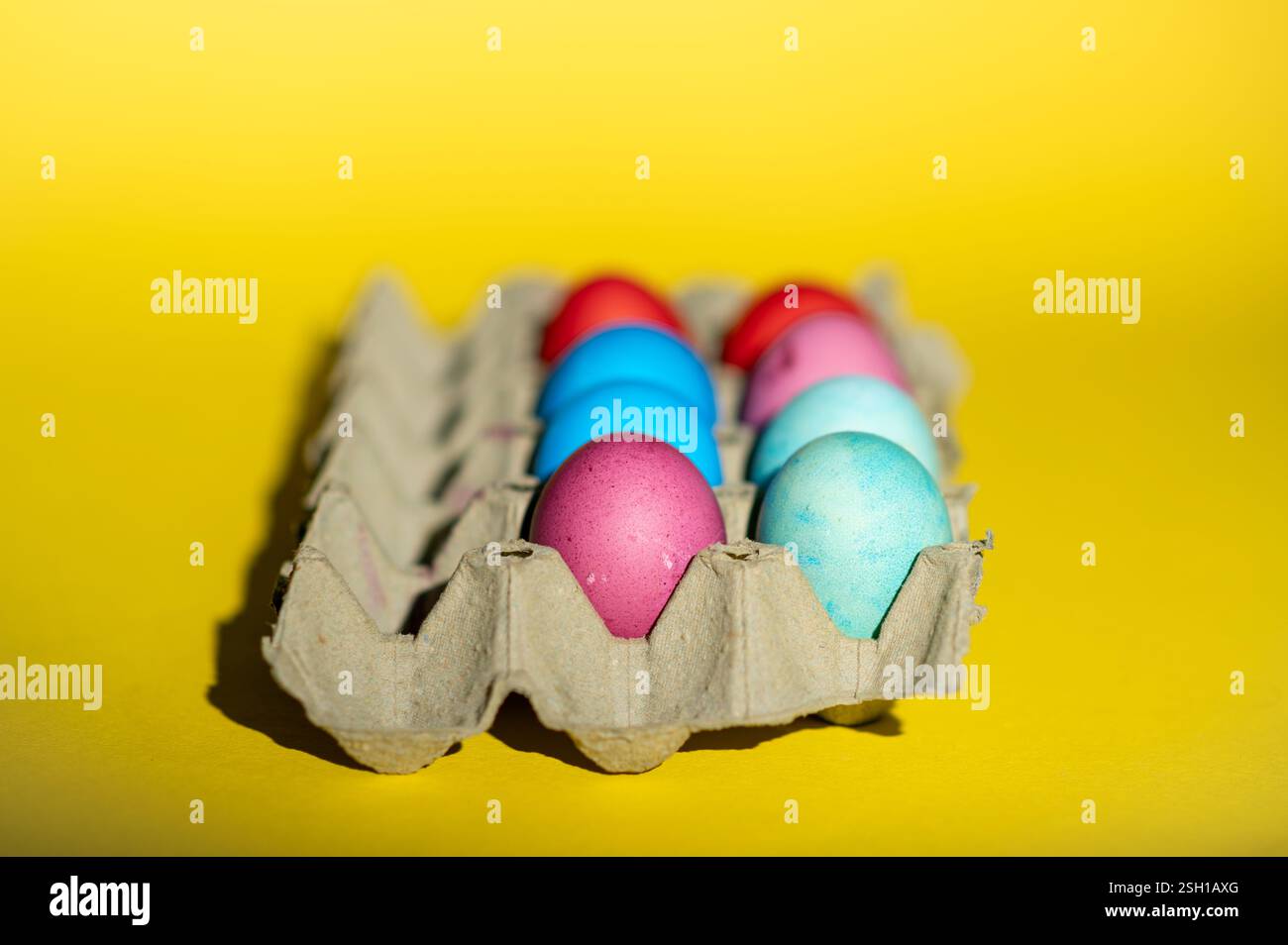 Colored Easter eggs in egg carton on the yellow background ready to be ...