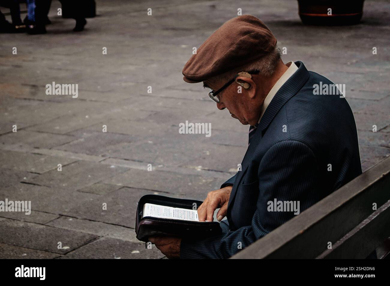 Elderly Man in a Suit with Hearing Aid Reading a Book on a Park Bench ...