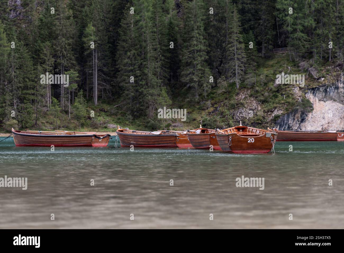 A detailed perspective of traditional wooden rowboats at Lake Braies, with pine trees and rocky ...