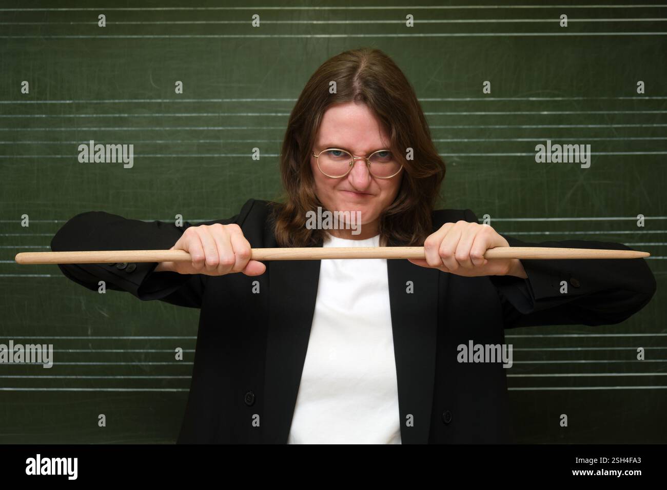 An angry teacher with glasses is standing in an empty classroom, her ...