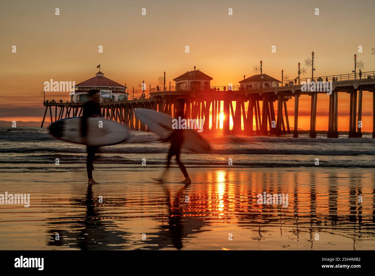 Two surfers walk the sandy shoreline of Huntington Beach during a ...
