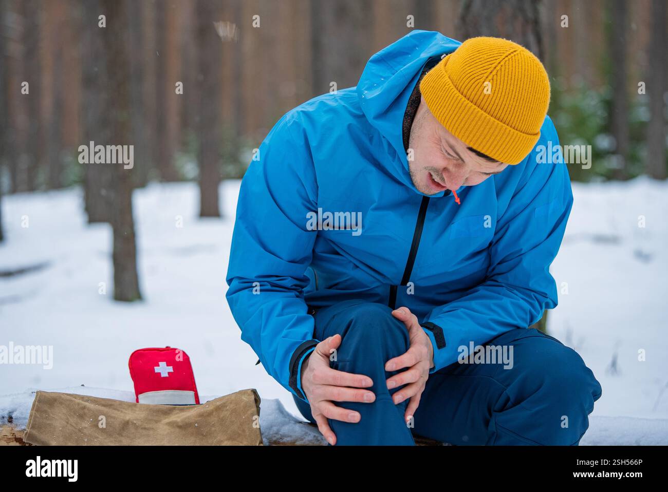 Male hiker feeling a sharp pain in his knee while sitting on a fallen ...