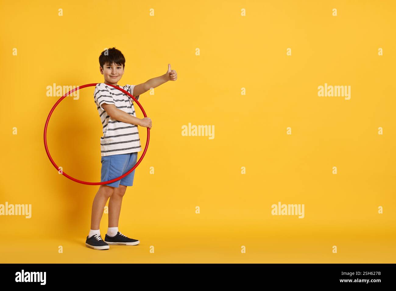 Boy with hula hoop showing thumbs up on yellow background, space for ...