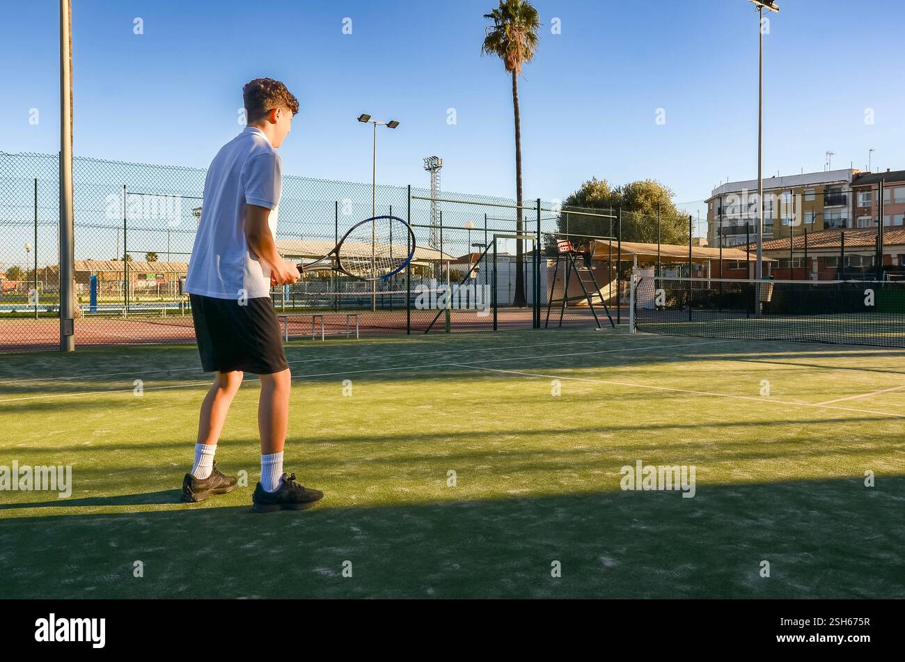 Teenager playing tennis, holding racket and getting ready to serve on a ...
