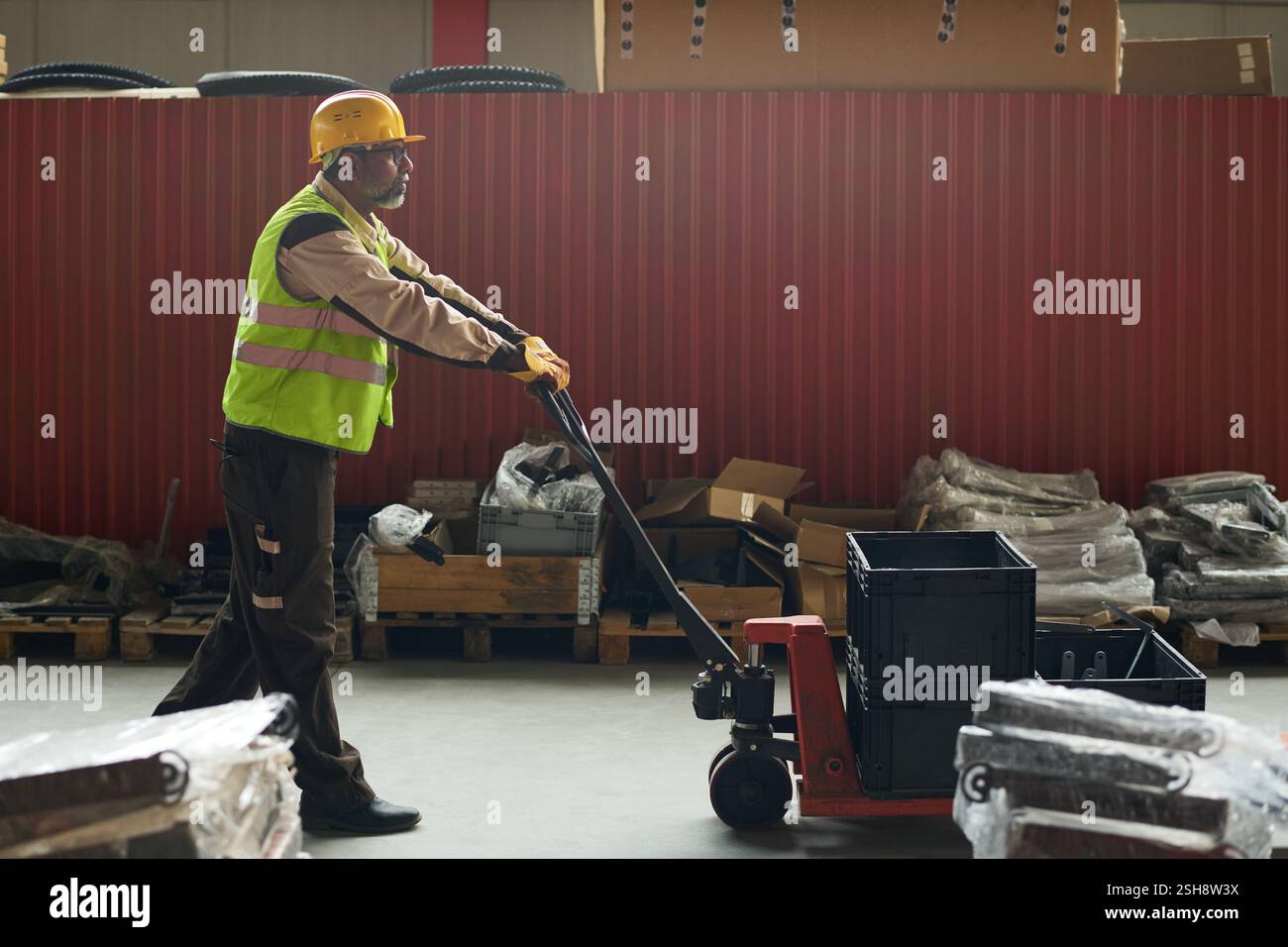 Side view of mature male engineer pushing pallet truck with stack of ...
