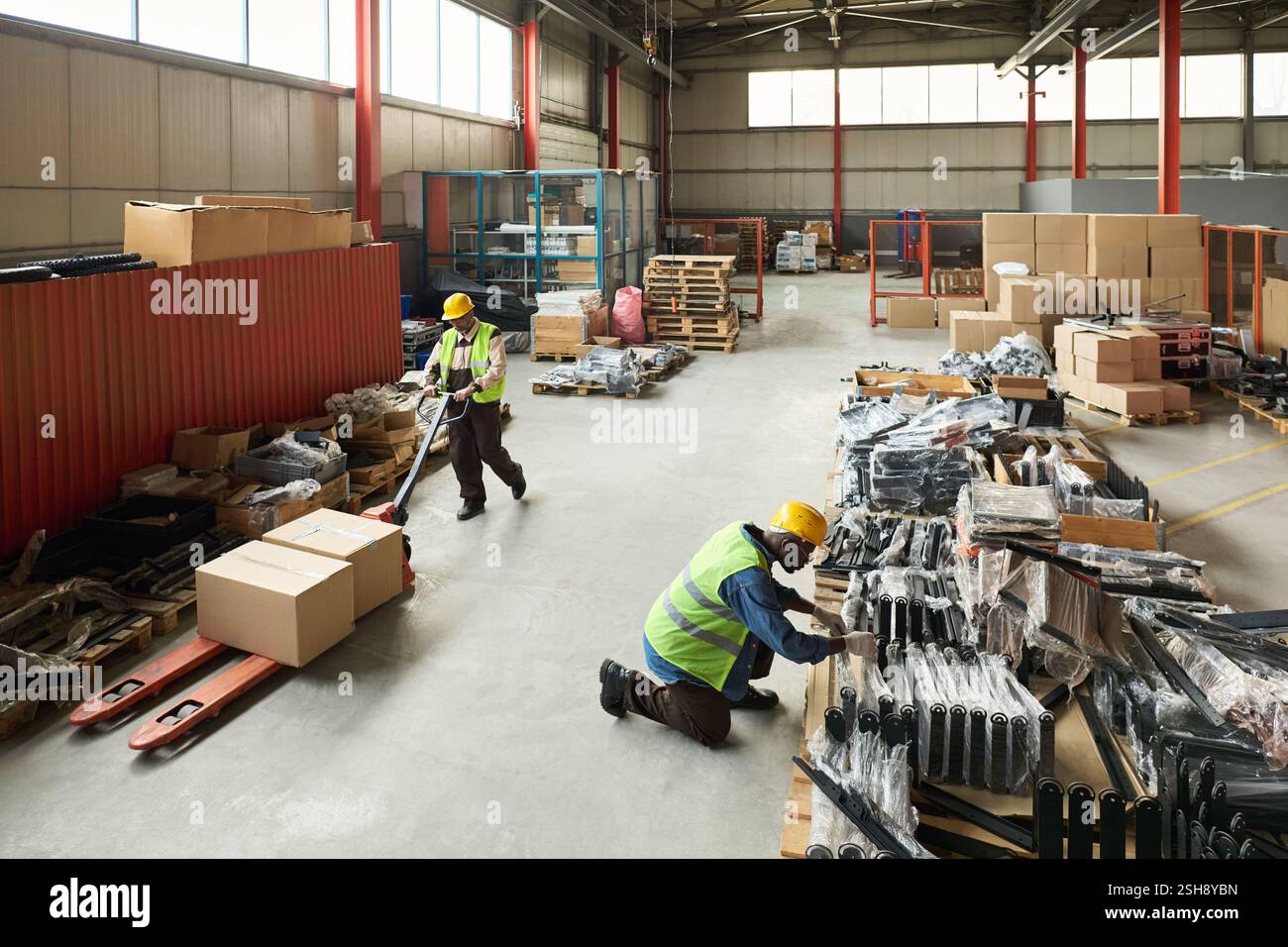 Mature worker pushing pallet truck with packed boxes while passing by ...
