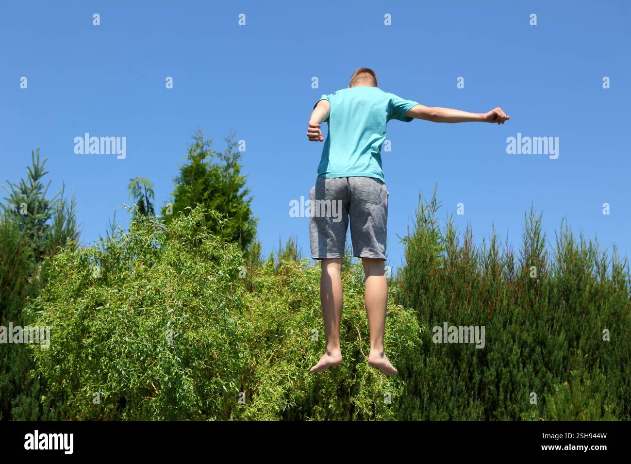 A boy is joyfully jumping high into the air over trees beneath a ...