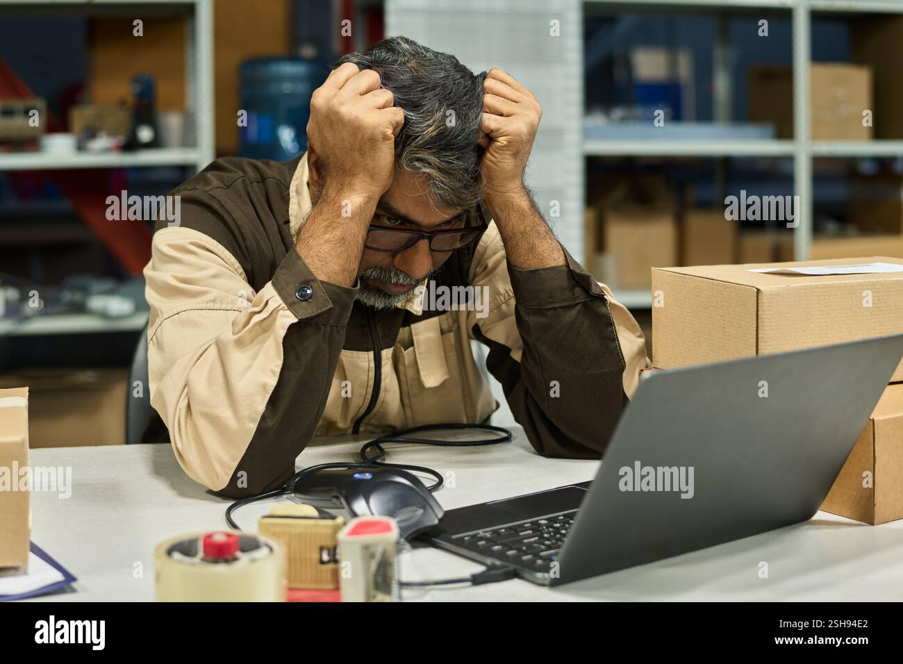 Tense and tired warehouse worker looking at laptop screen during ...