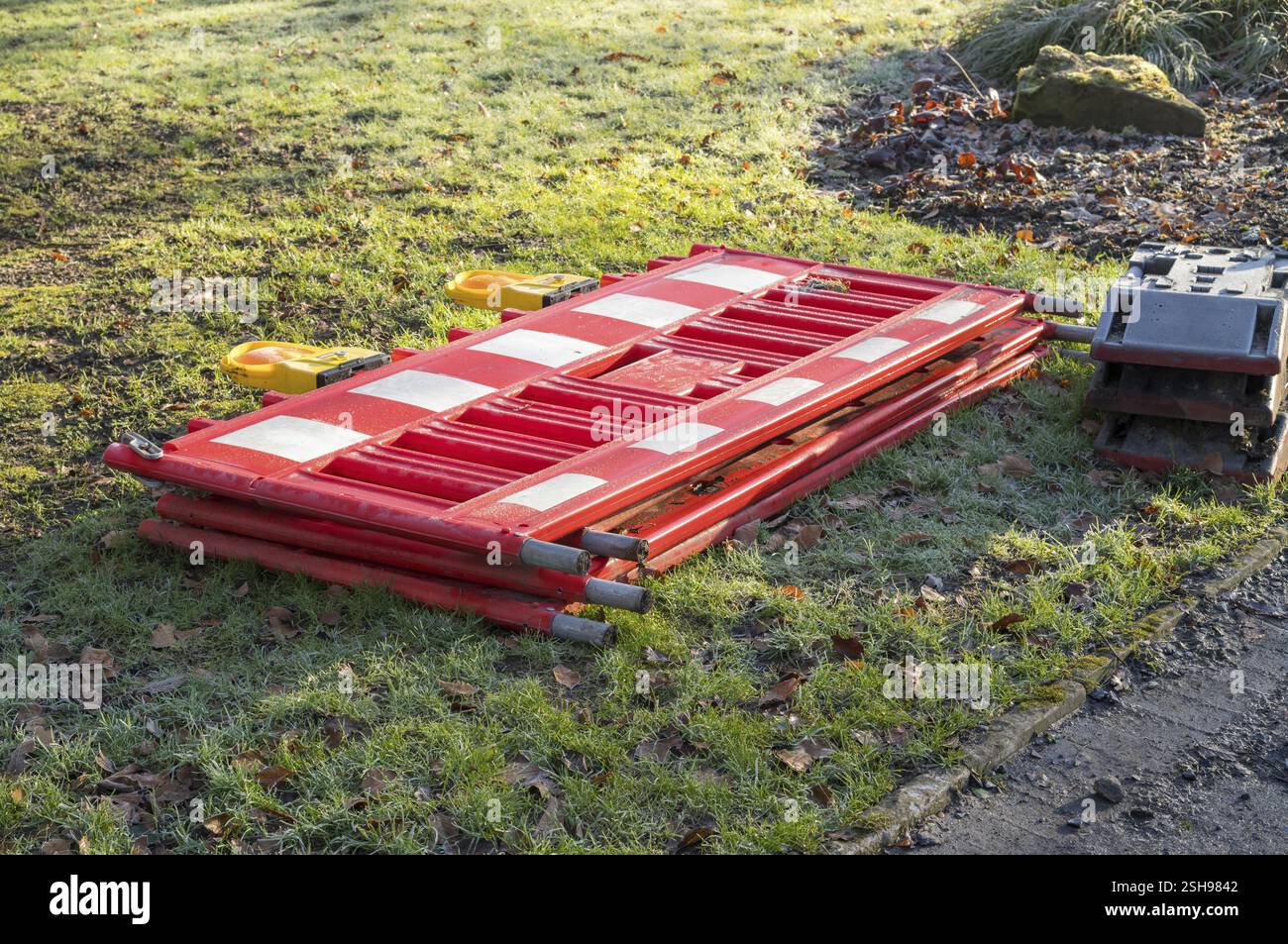 Red and white metal crowd control barriers laying stacked on grass next ...