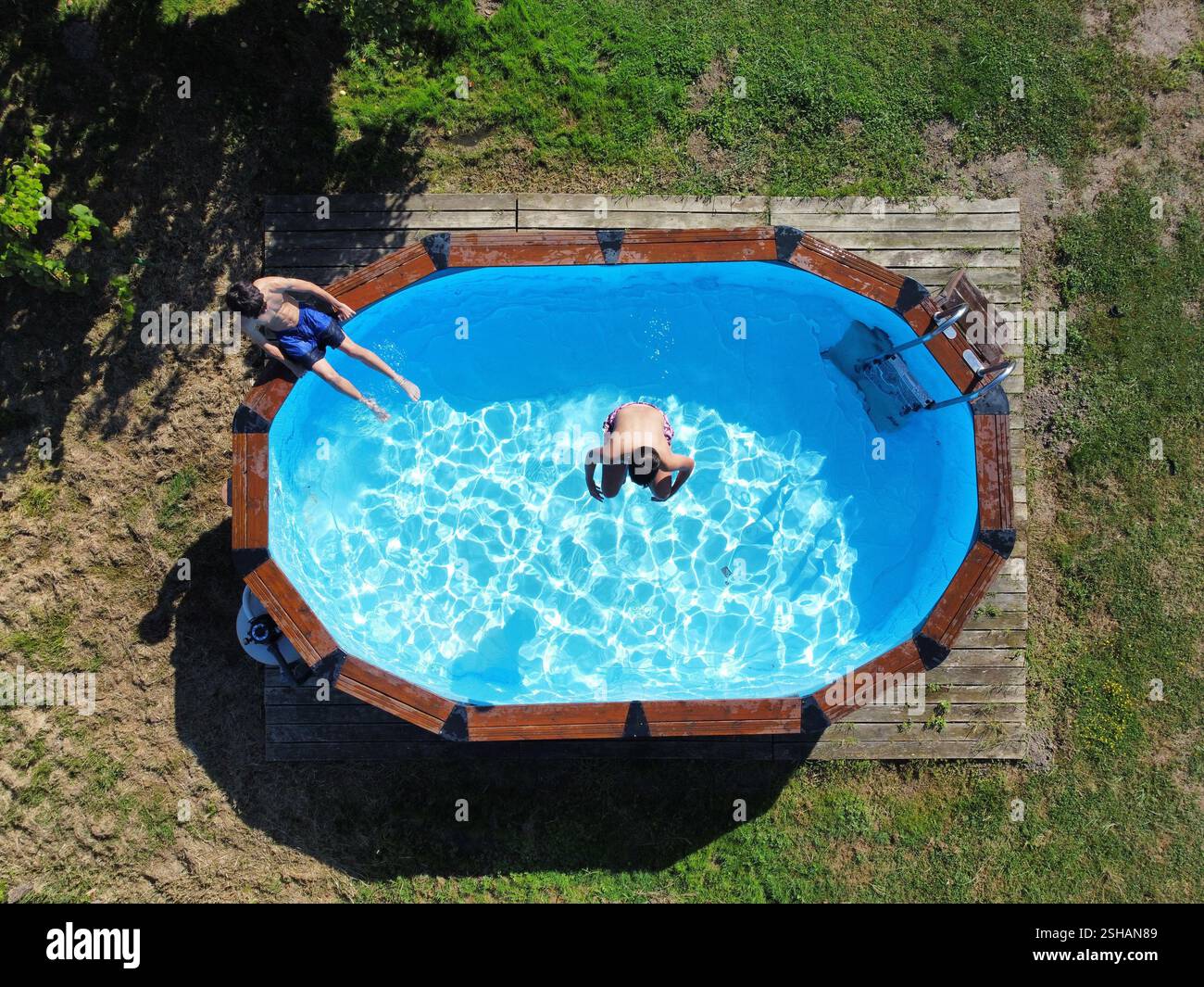 drone view of two teenagers bathing in a portable swimming pool, one sits on the edge watching ...