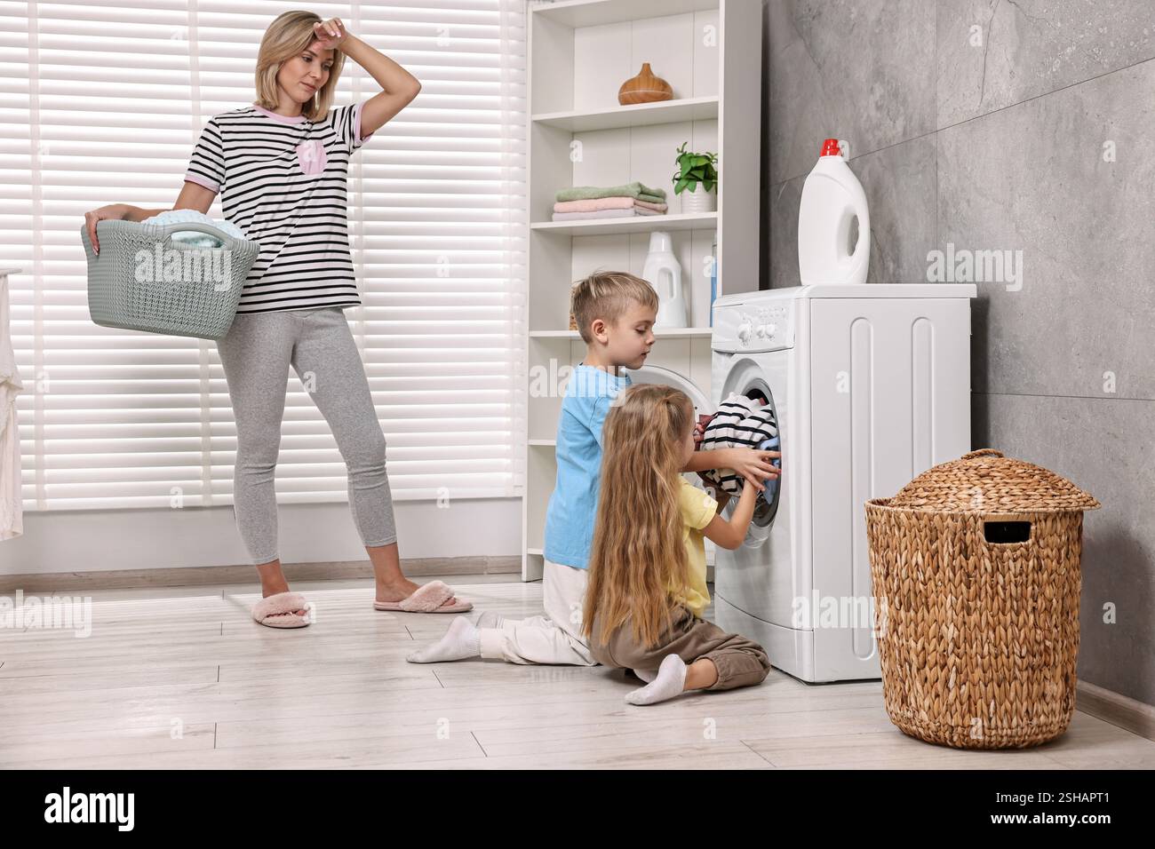 Tired housewife and her kids doing laundry together in bathroom Stock Photo - Alamy