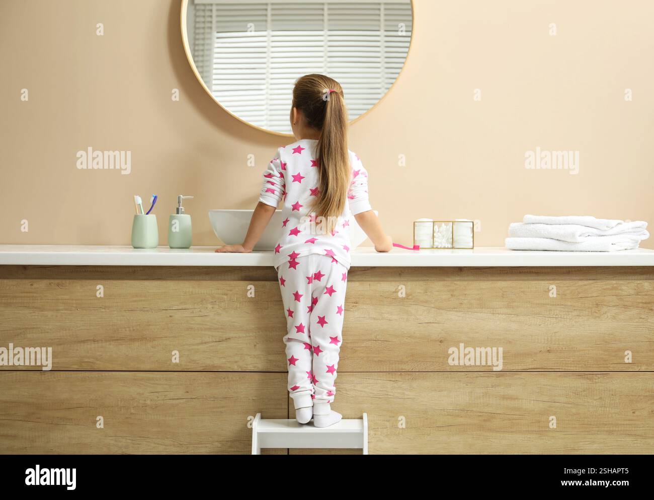 Little girl with toothbrush standing on step stool near bathroom vanity ...