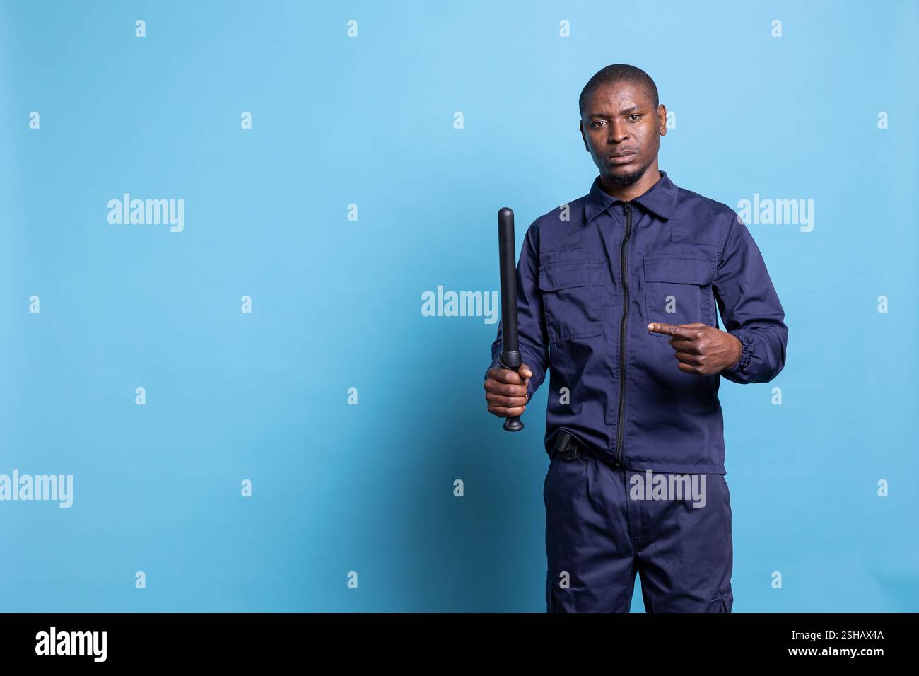 Trained security guard pointing at his baton against blue background ...