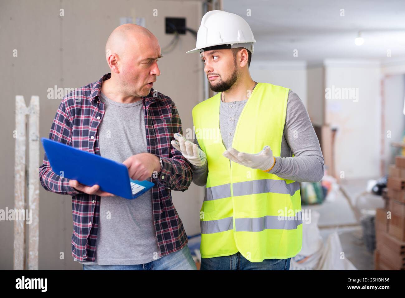Puzzled builder talking with displeased man with laptop in home during ...