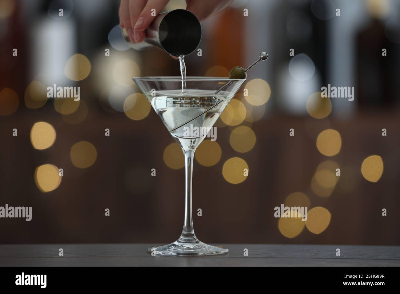 Woman making tasty martini cocktail with olives at wooden table on ...
