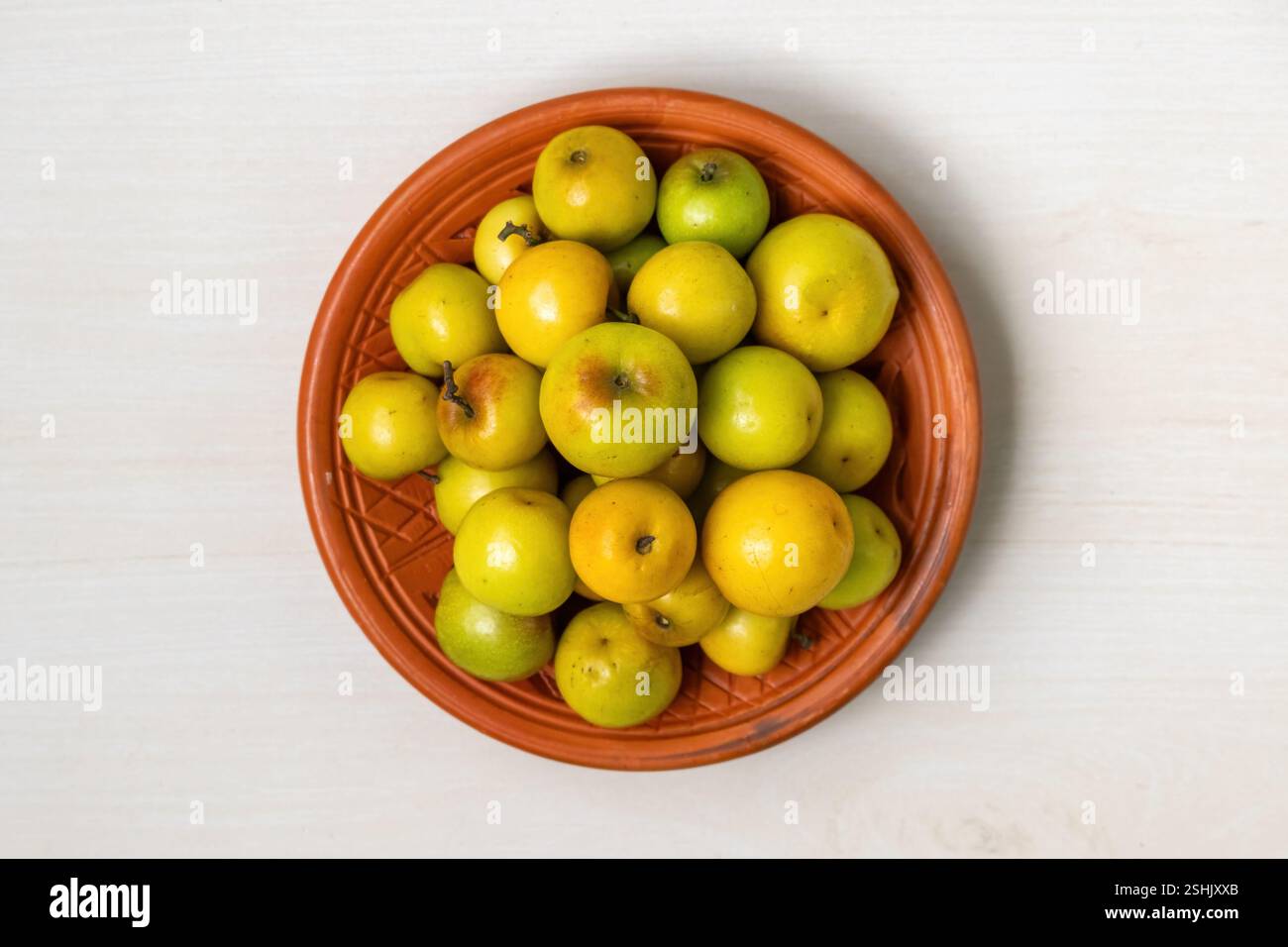 Fresh ripe plum fruits on a clay plate on a wooden background. Locally ...