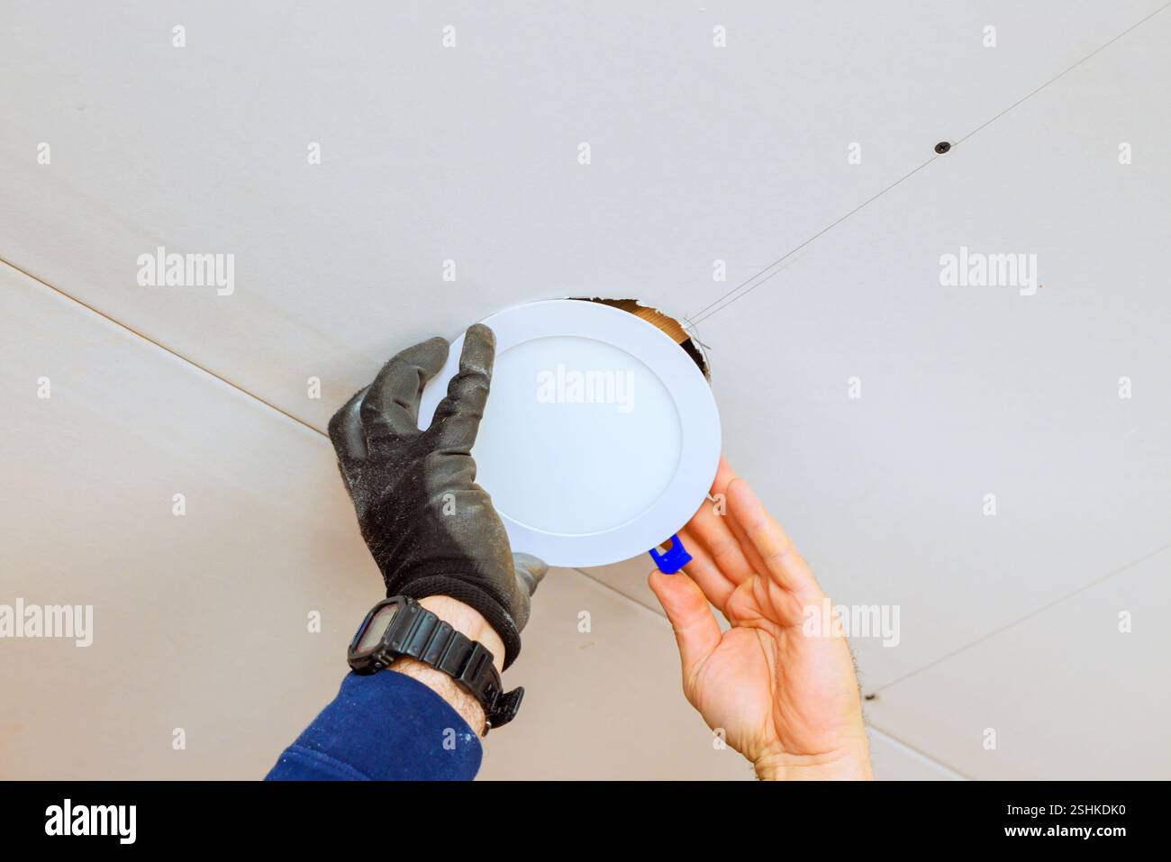 An electrician is carefully placing recessed light fixture into ceiling ...