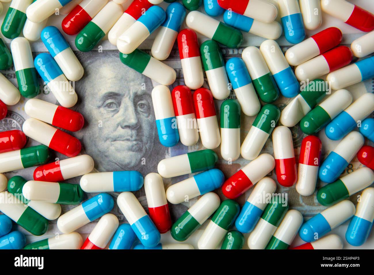 A close-up image of colorful capsules scattered on a US dollar bill ...