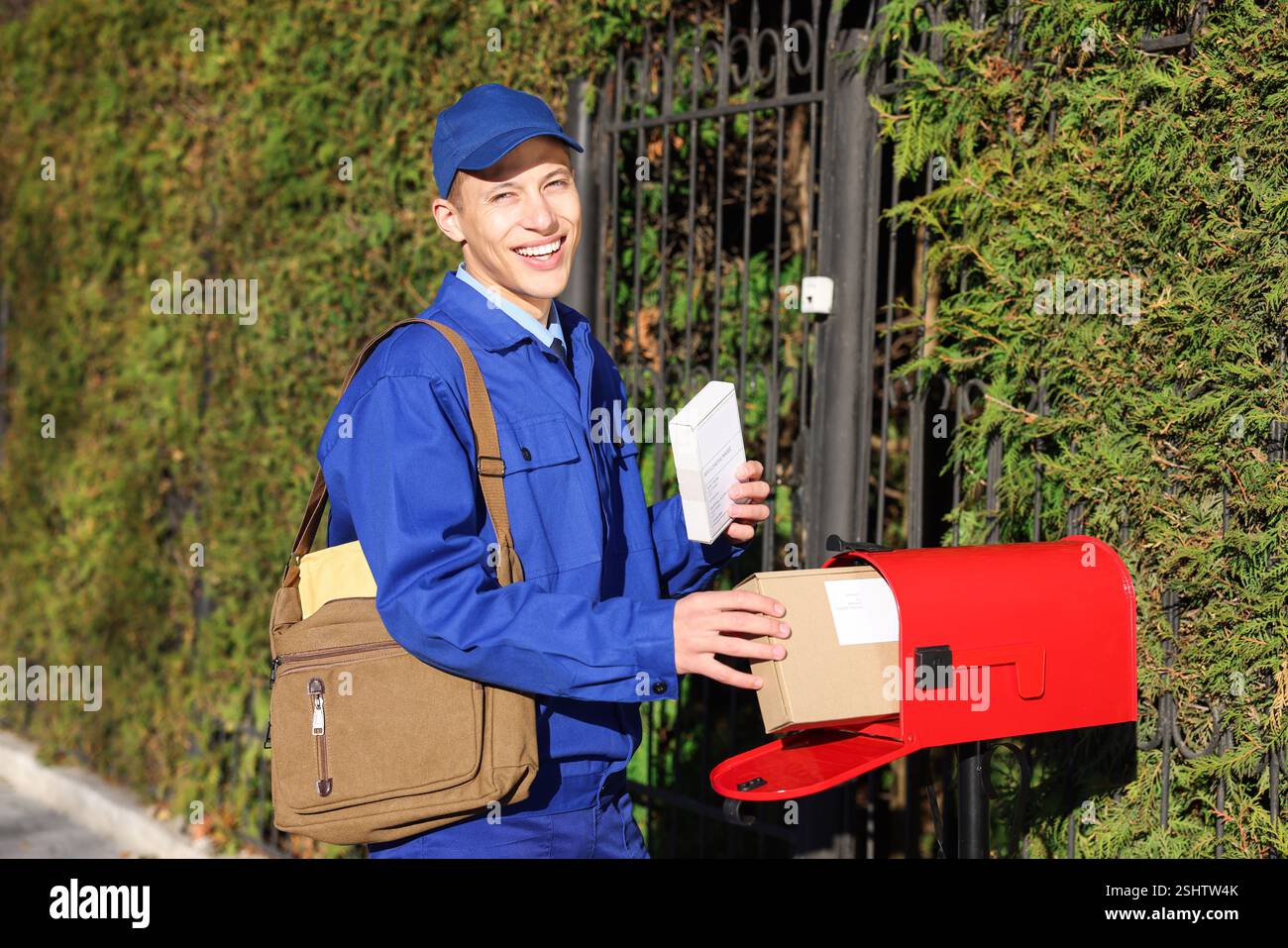 Postman putting parcel into mail box outdoors Stock Photo - Alamy